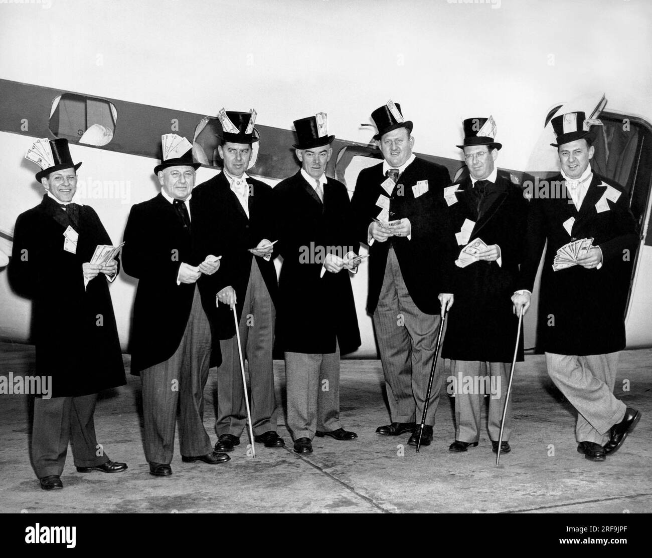 United States: c. 1954. Seven men in tuxedos and top hats with handfuls ...