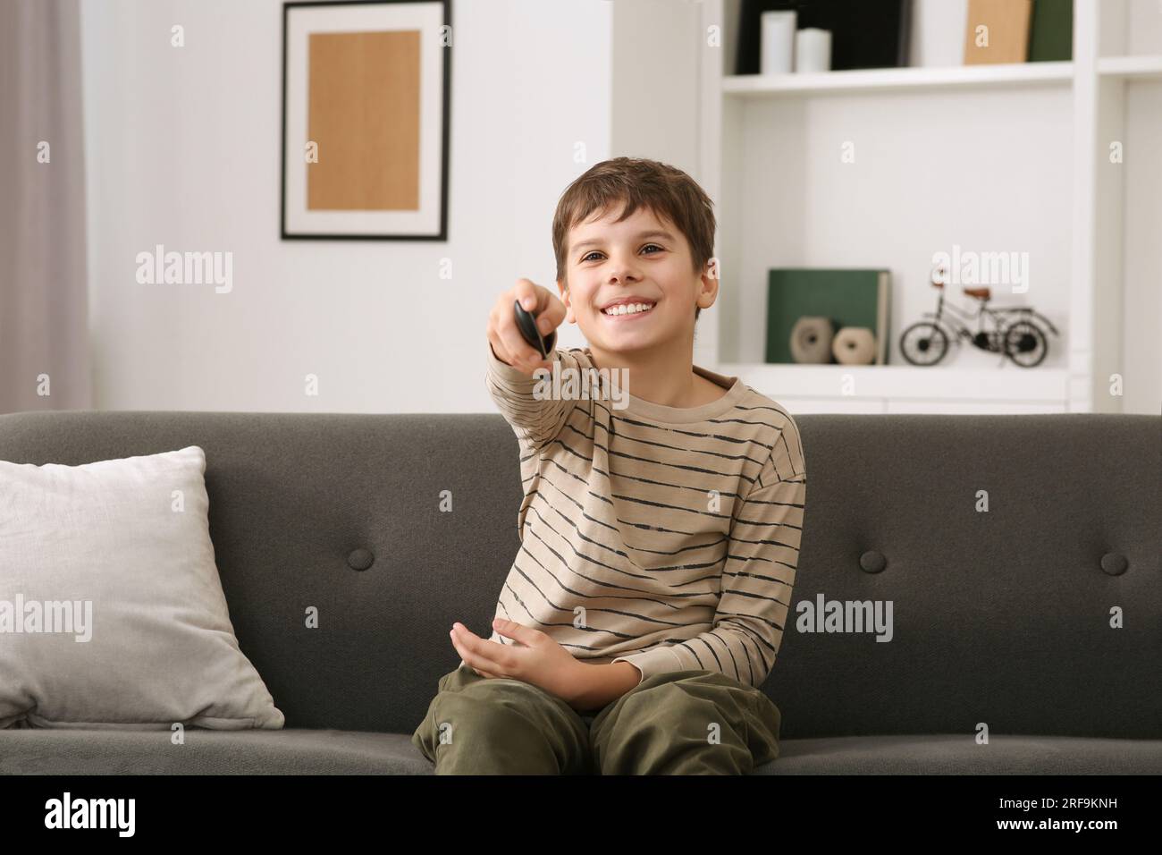 Happy boy changing TV channels with remote control on sofa at home ...