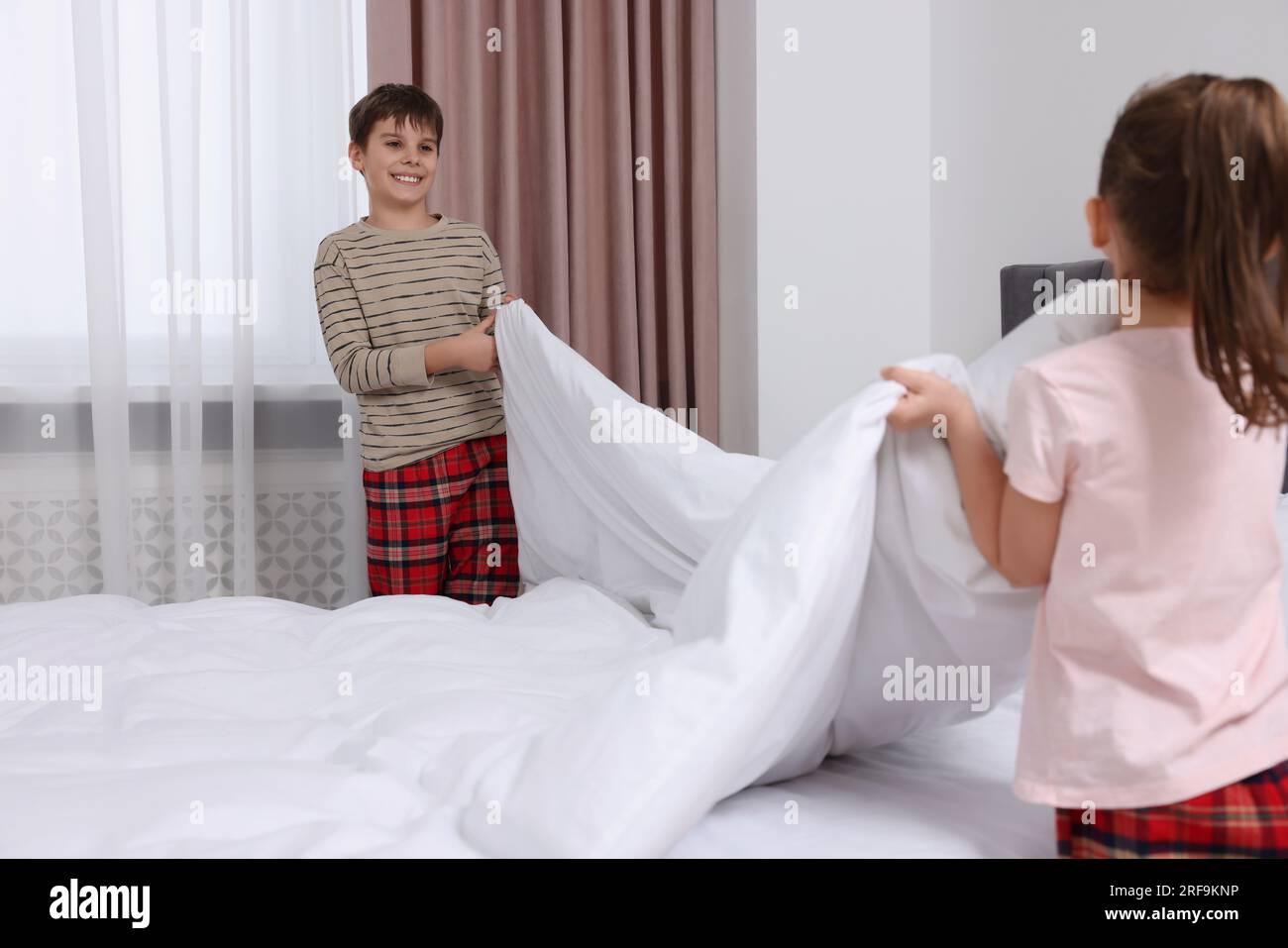 Brother and sister changing bed linens together in bedroom Stock Photo ...