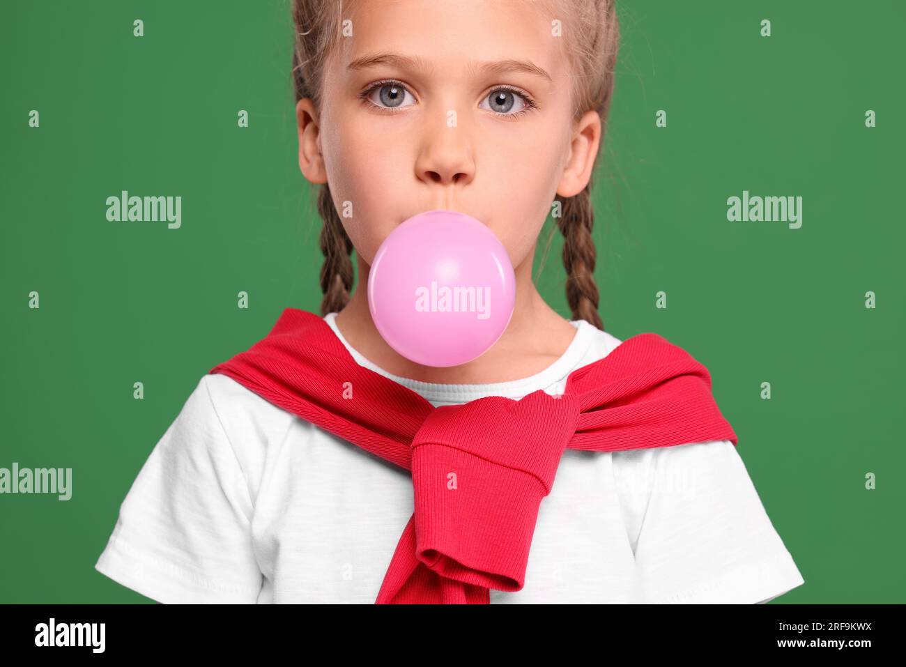 Girl blowing bubble gum on green background Stock Photo - Alamy