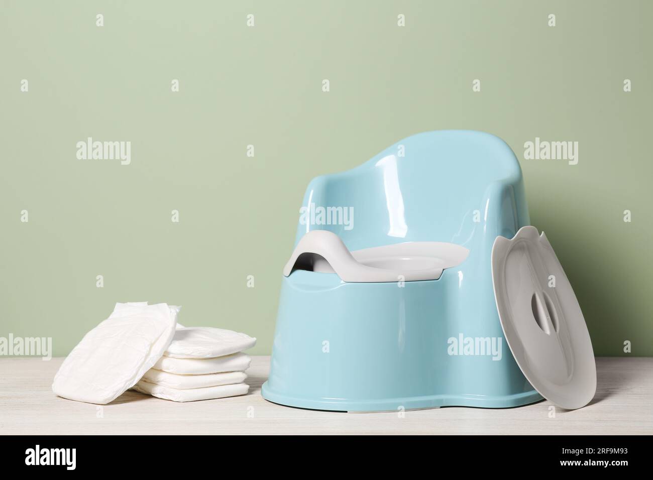 Light blue baby potty and diapers on white wooden table against olive ...