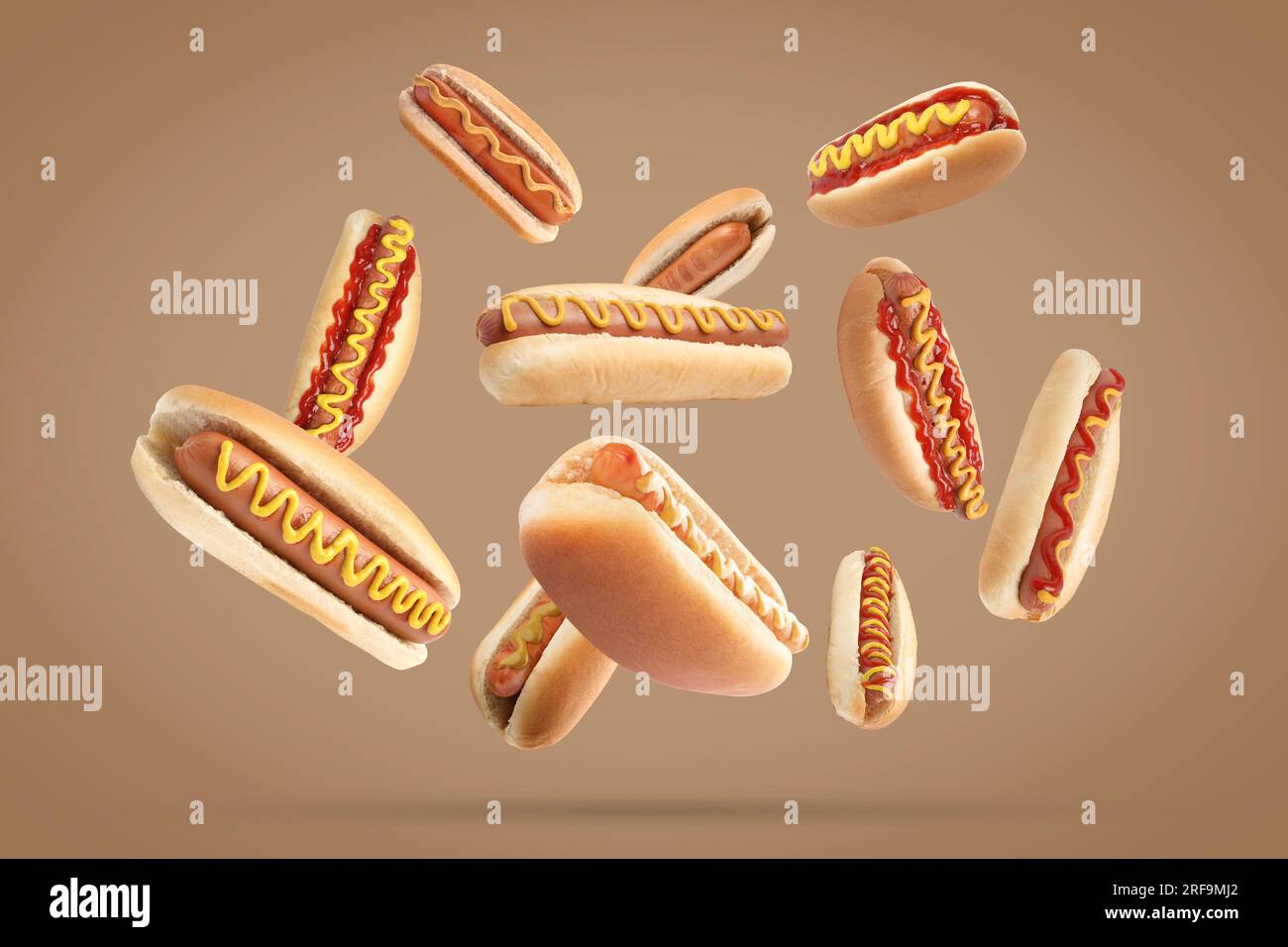 Many tasty hot dogs falling on pale brown background Stock Photo - Alamy