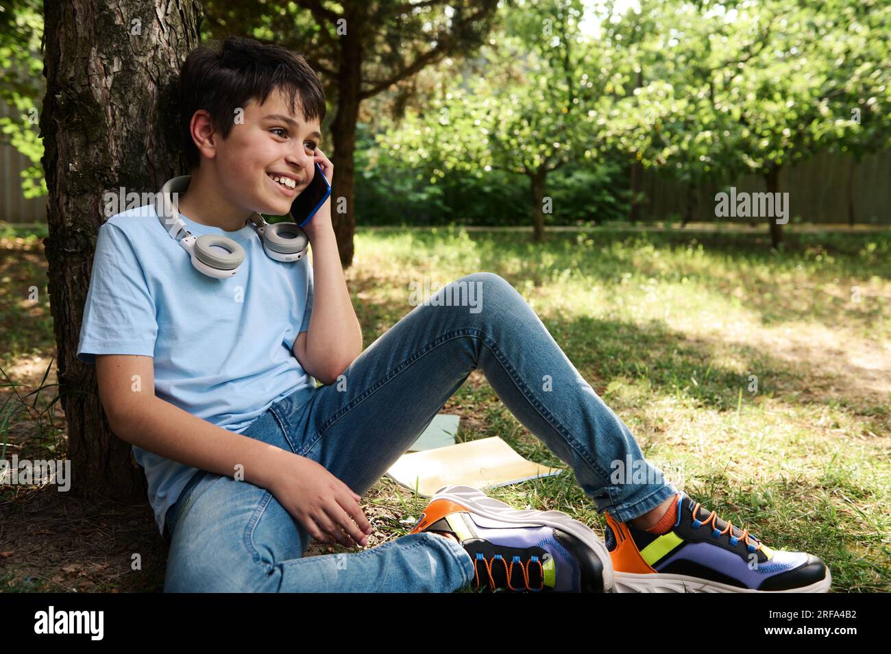 Cheerful handsome teen boy talking on mobile phone, wearing headphones ...