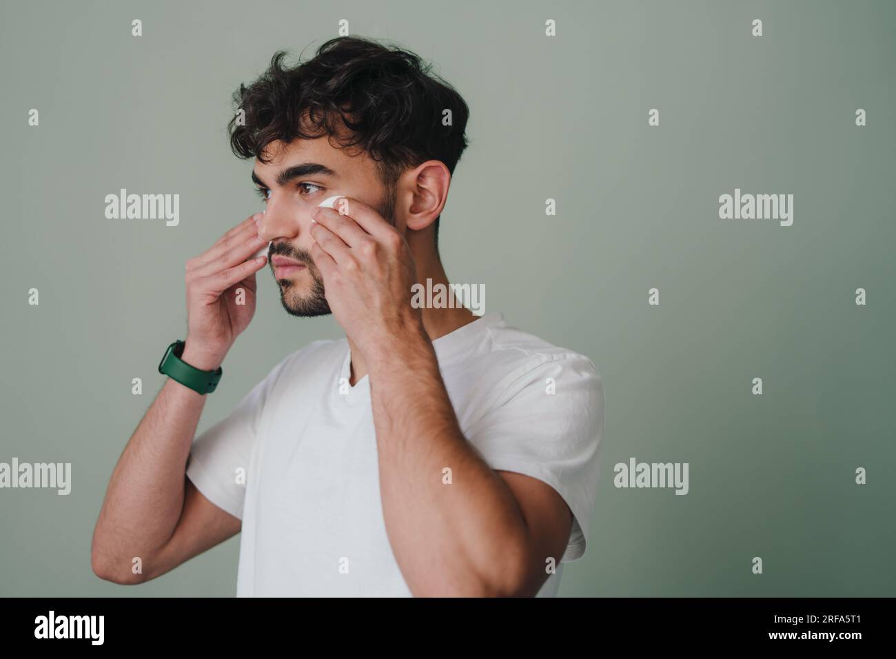 Young handsome man is cleaning his face with a cotton pads on isolated ...