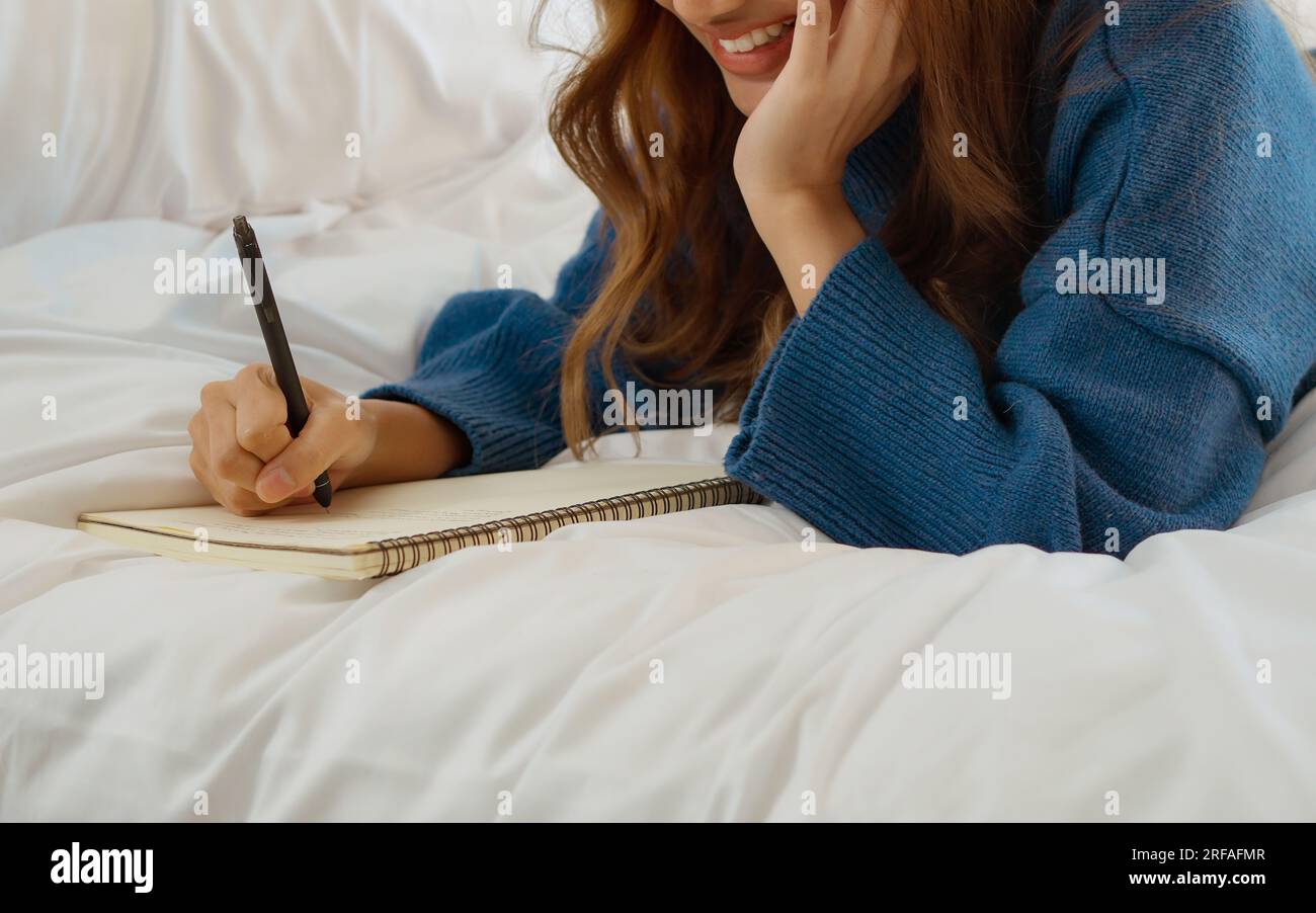 Happy young woman laying on bed and writing in journal at bedroom Stock ...