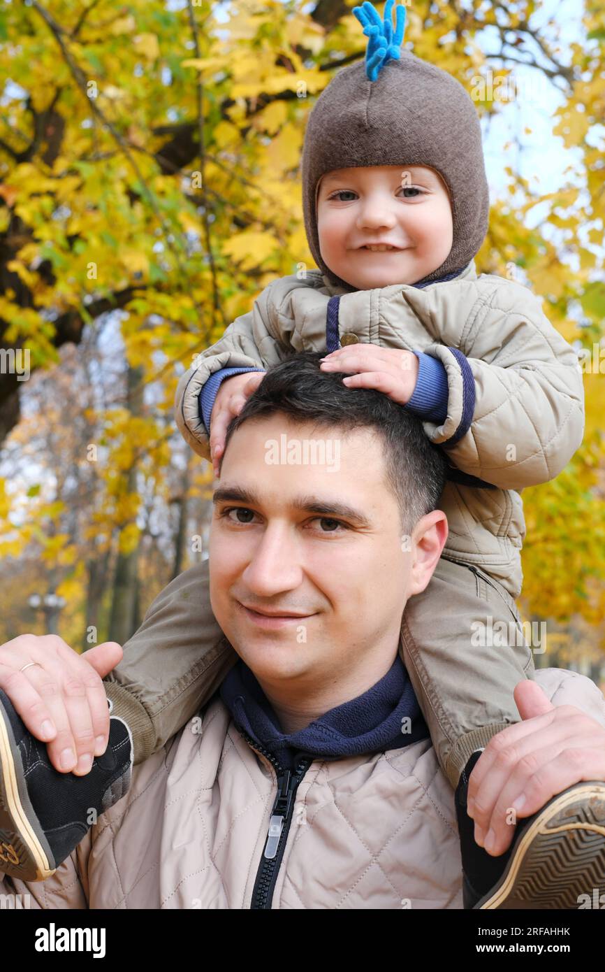 Portrait of a father carrying his cute little son on shoulders, baby ...