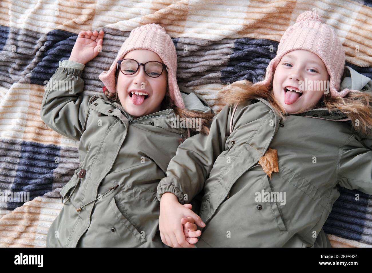 Two happy twin sisters lie on a blanket in an autumn park. The girls ...