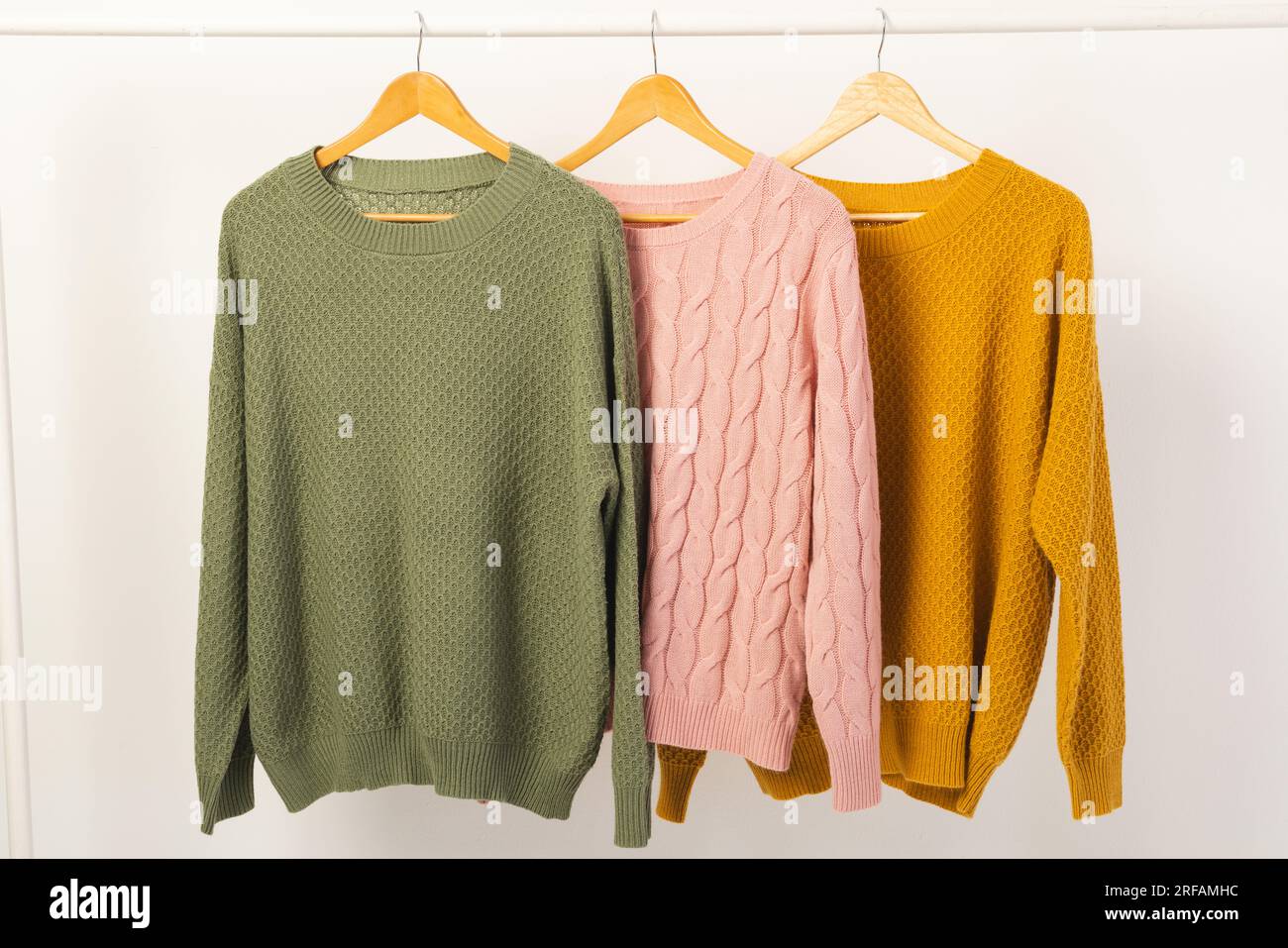 Three sweaters hanging from clothes rail with copy space on white ...