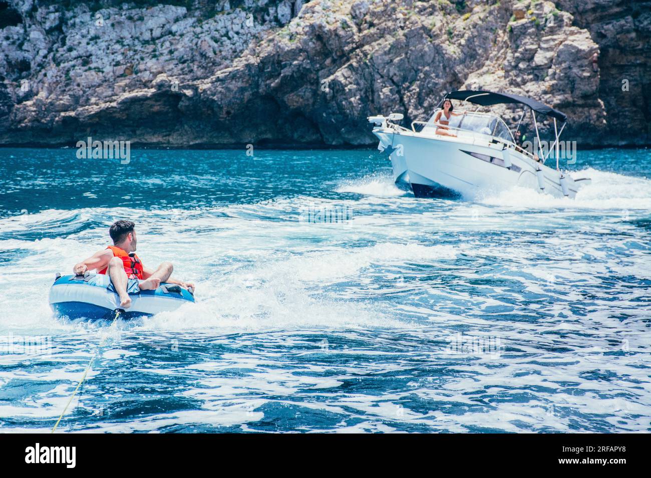 Young man on an inflatable donut, pulled by a boat at sea, looking back ...