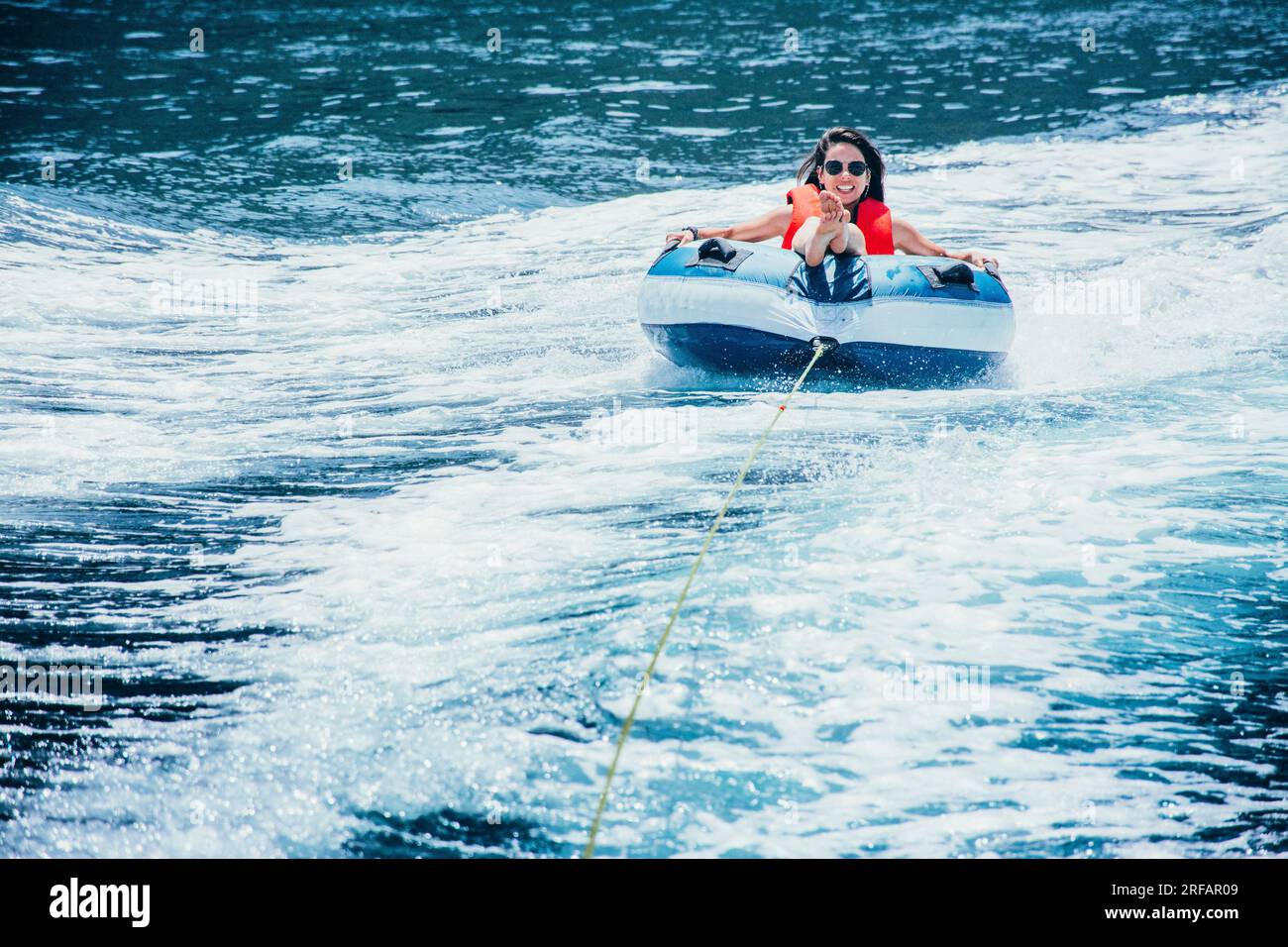 Smiling young woman enjoying surfing the sea sitting on an inflatable ...