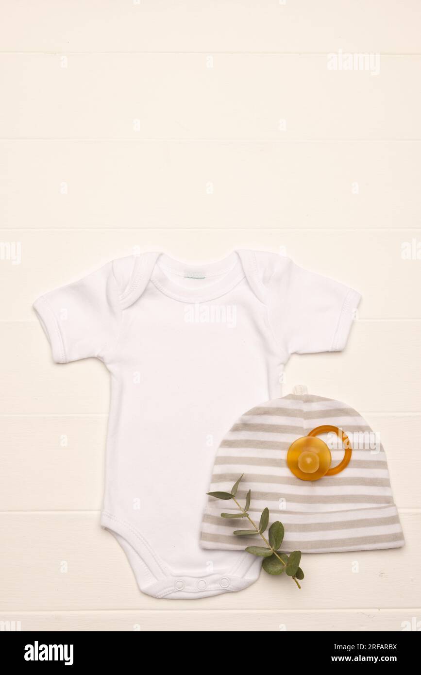 Flat lay of white baby grow, hat and dummy with copy space on white ...