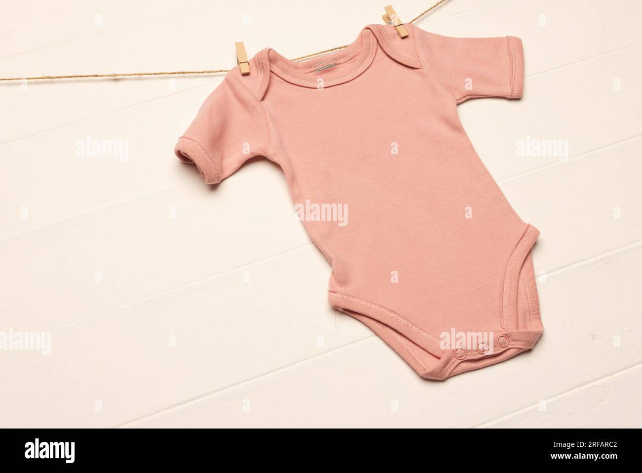 Pink baby grow hanging with clothes pegs with copy space on white ...