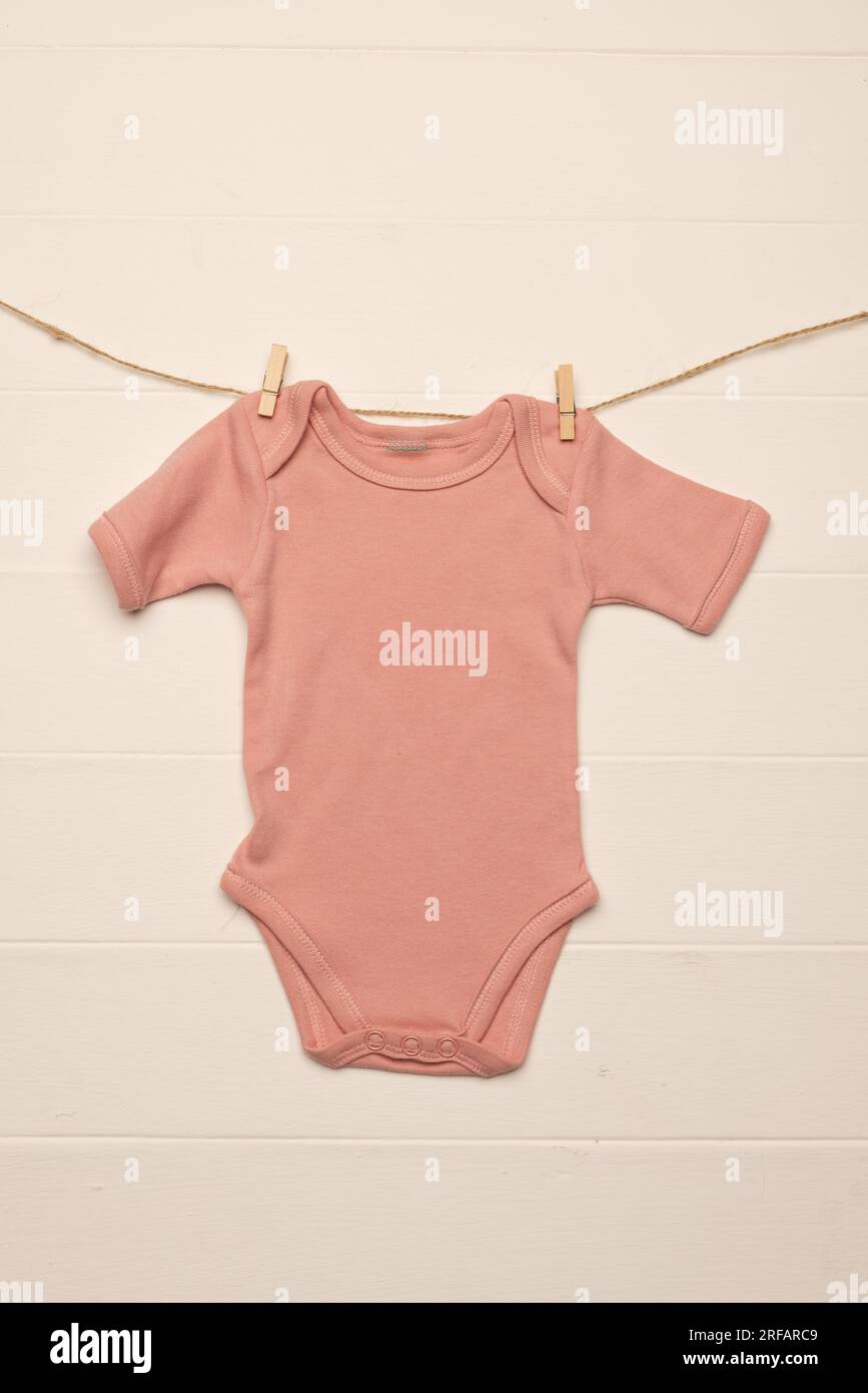 Pink baby grow hanging with clothes pegs with copy space on white ...