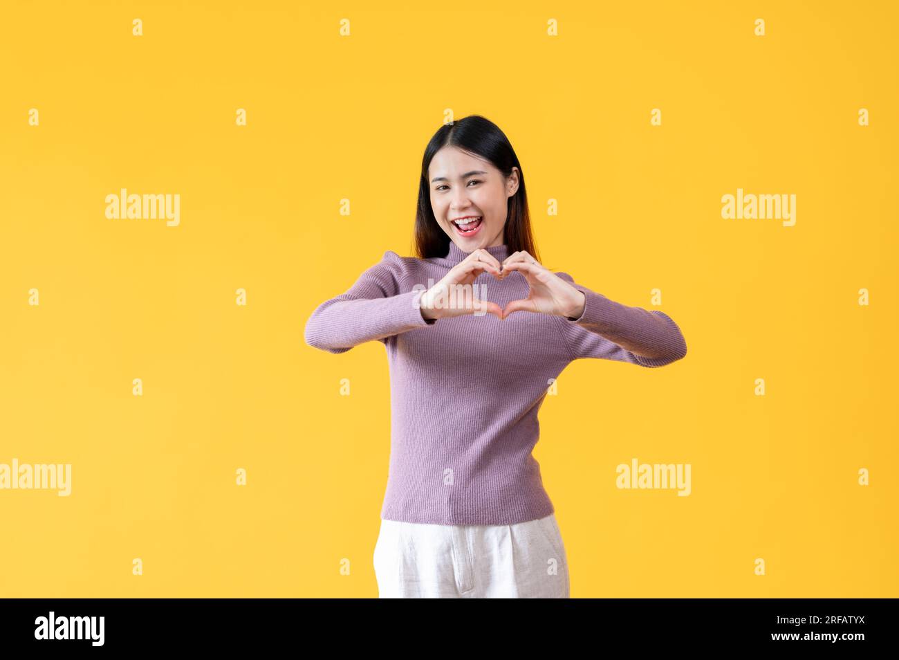A pretty and smiling Asian woman in casual clothes is making the heart ...