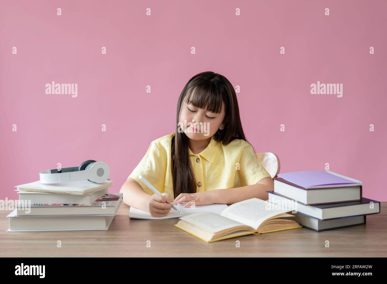 An adorable young Asian girl is focusing on her homework at her study ...
