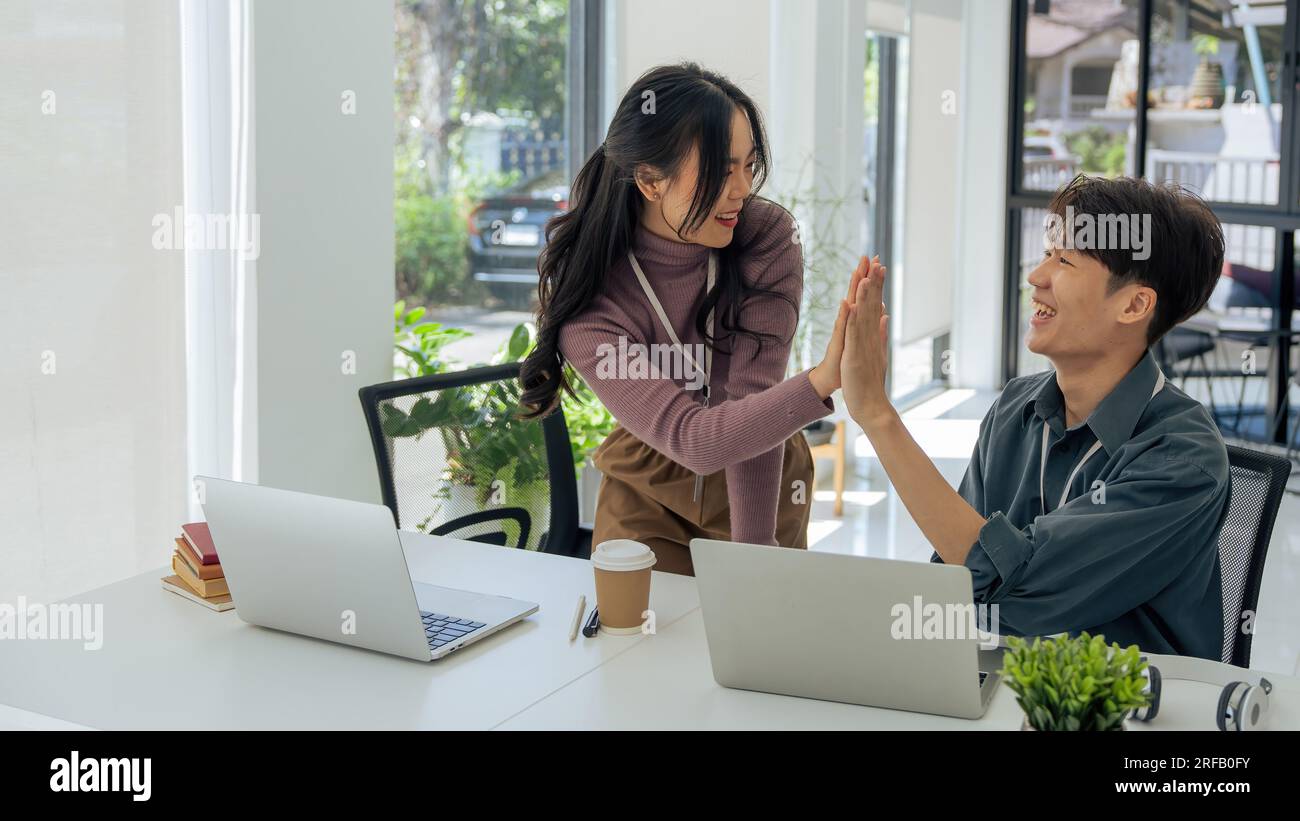 happy Asian female office worker gives high fives to a male colleague ...