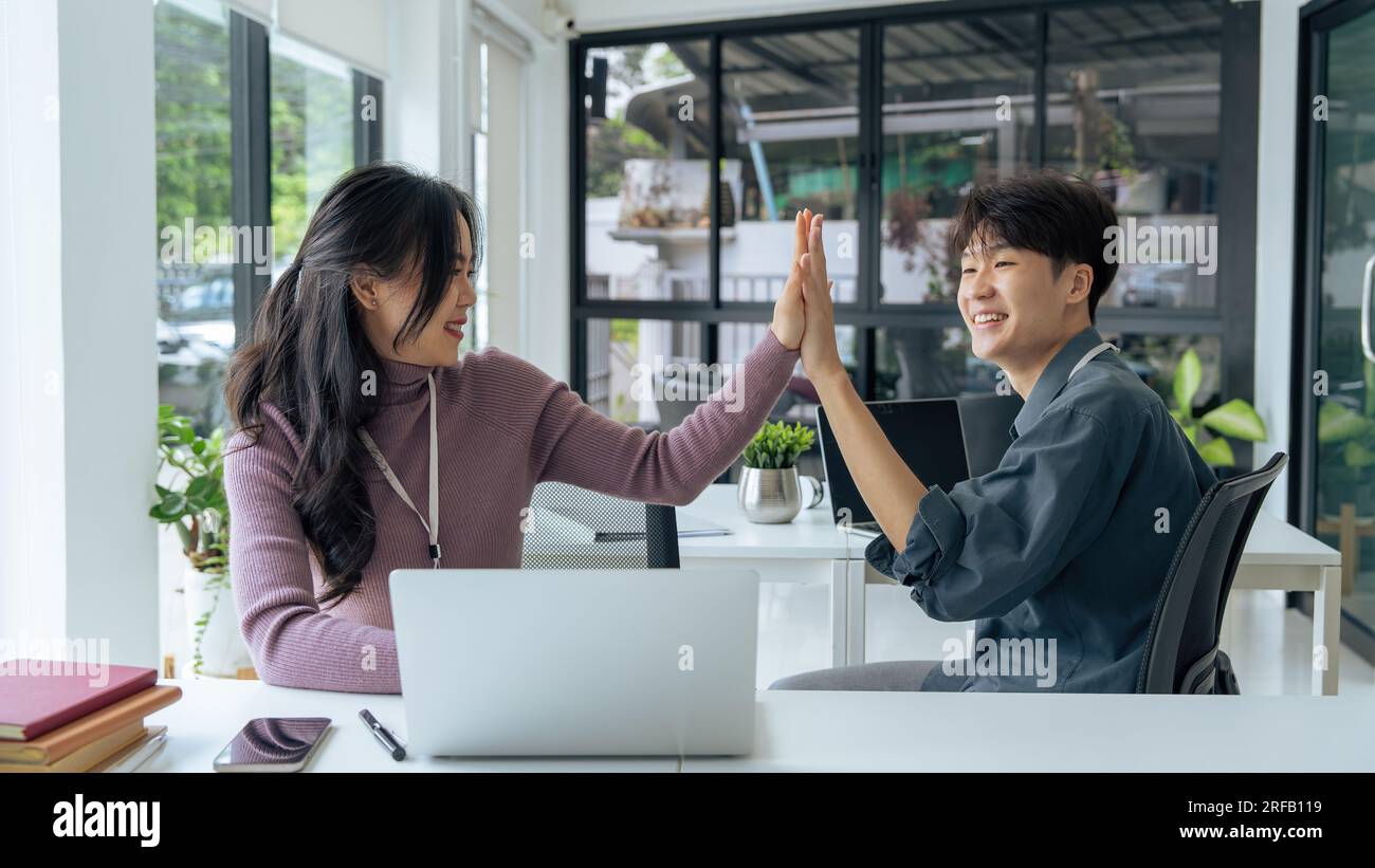 happy Asian female office worker gives high fives to a male colleague ...