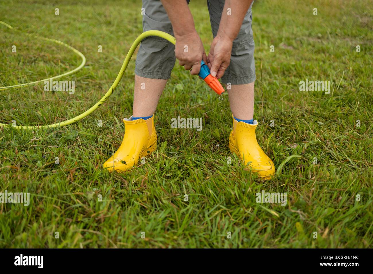 Close-up of a woman's hands washes yellow rubber boots from mud with a ...