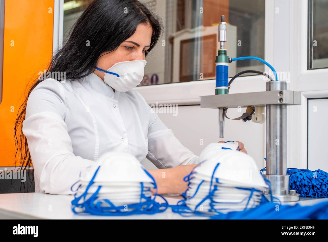 The girl works at the machine for the manufacture of medical masks with ...
