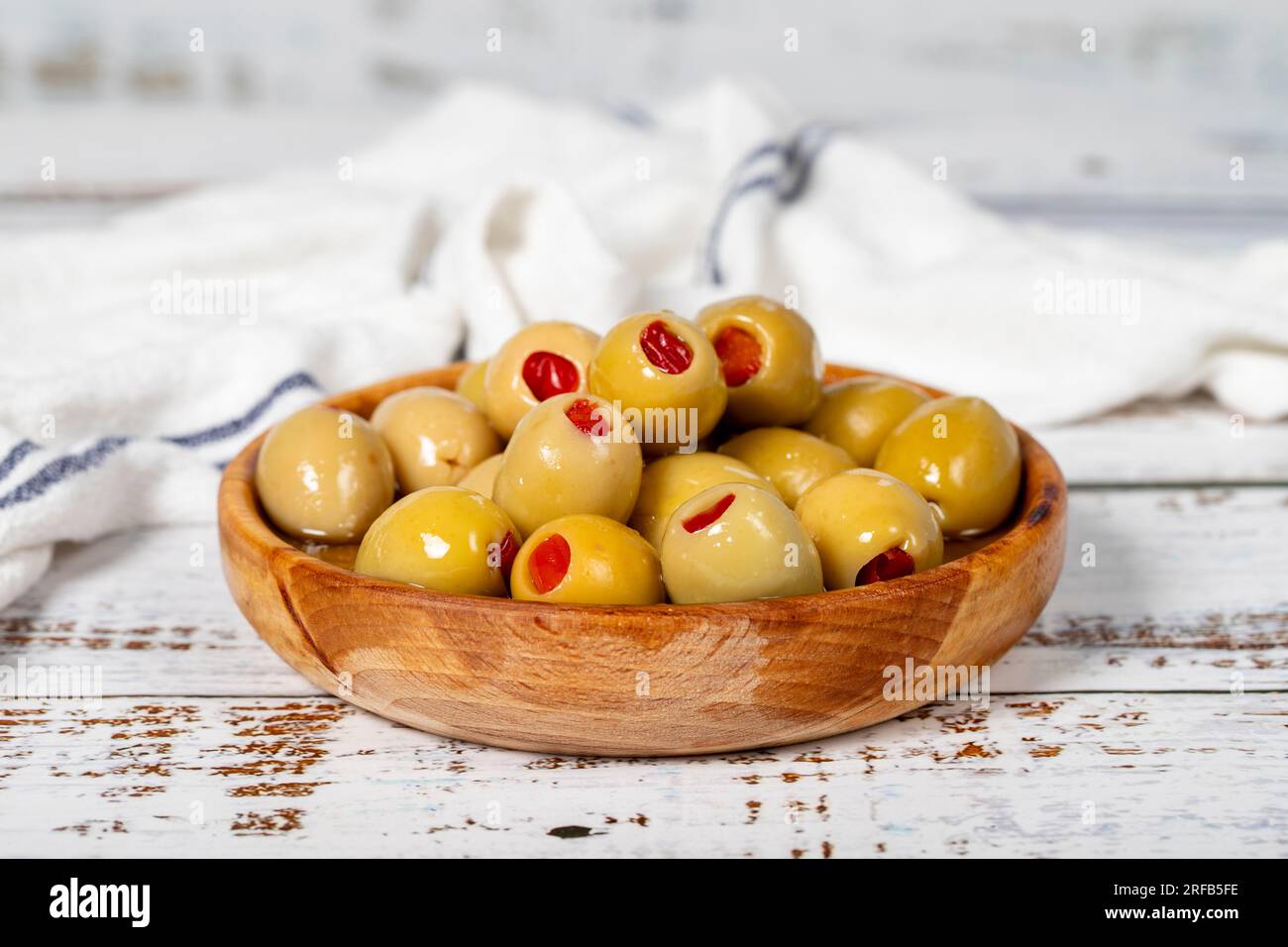 Pepper-stuffed green olives at wooden bowl. Olives on a white wood ...
