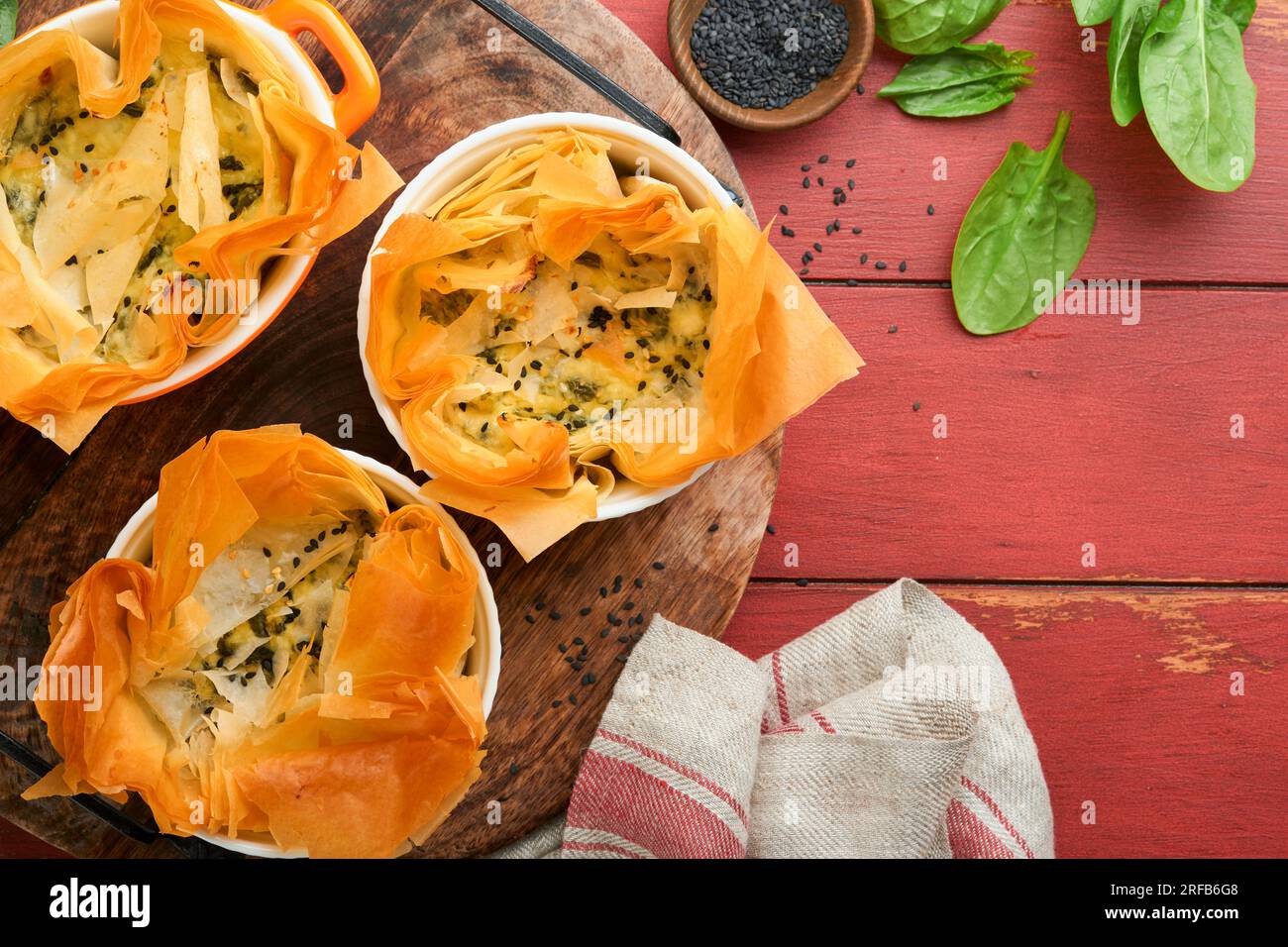 Filo pies with soft feta cheese and spinach in ceramic molds on old red ...