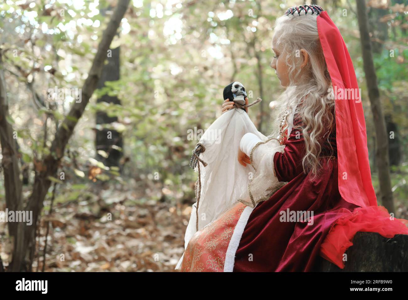 A child girl sits on a stump in the forest in a medieval dress in the ...