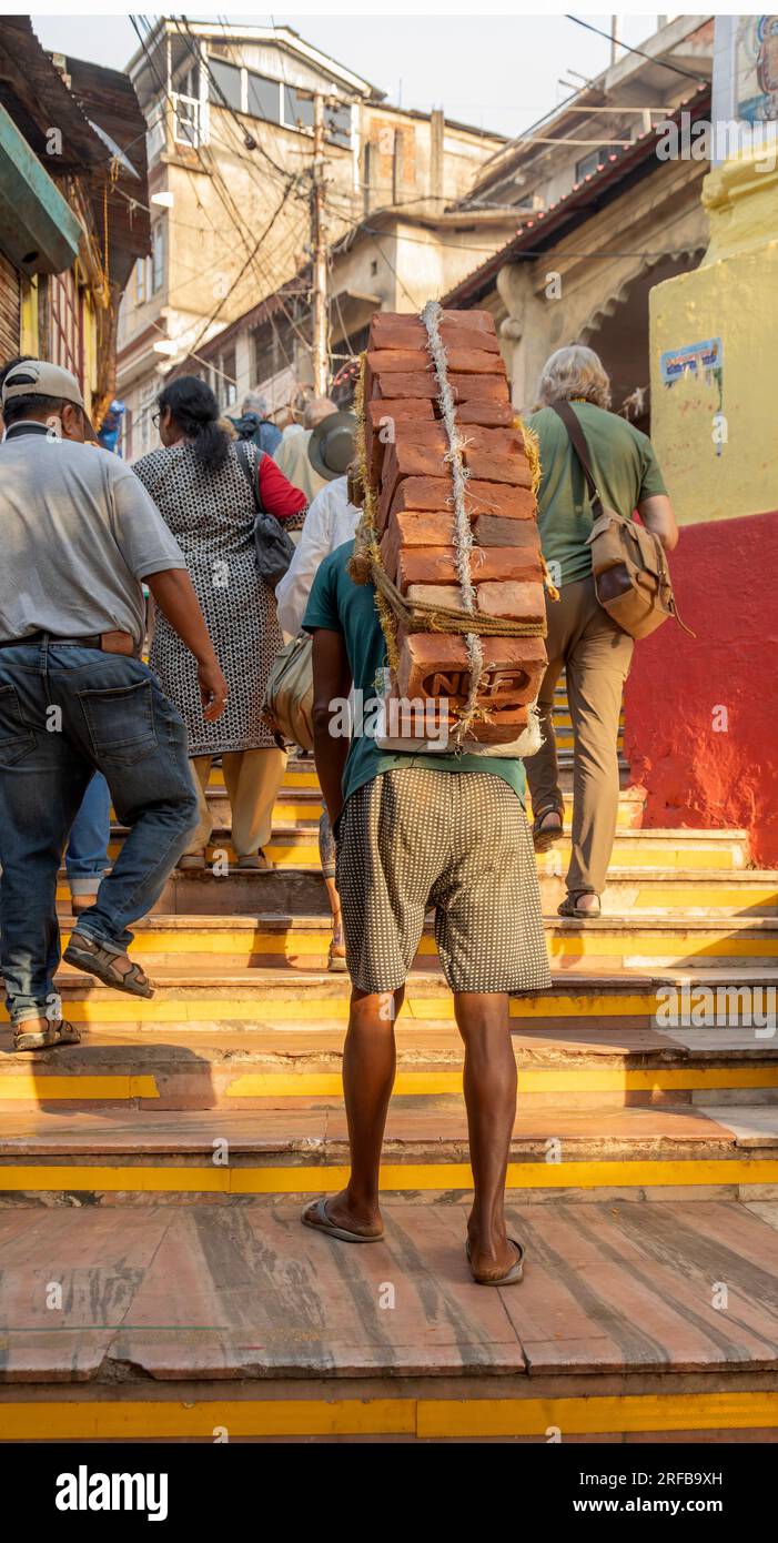A man wearing flip-flops and carrying a load of bricks on his back ...