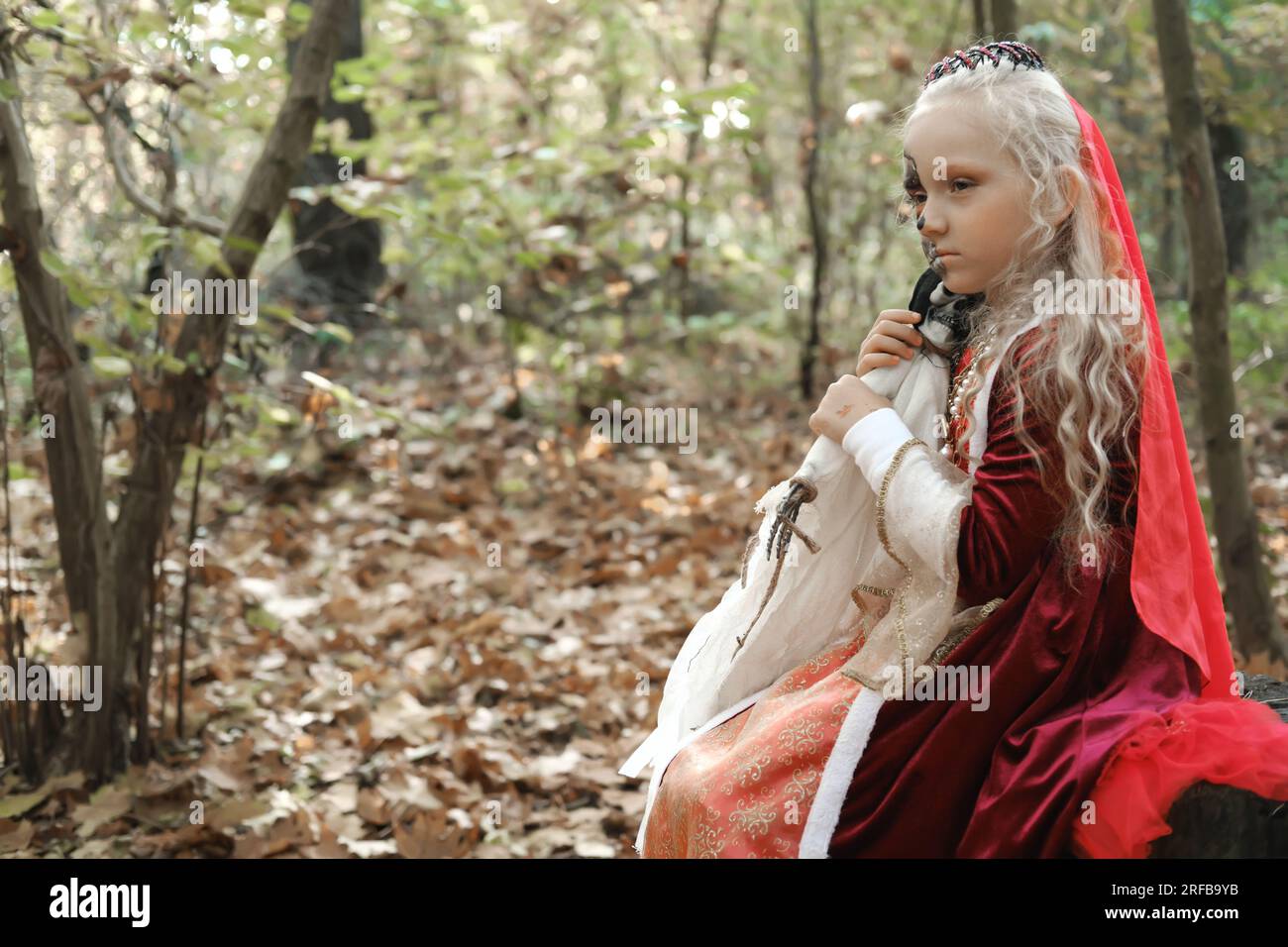 A child girl sits on a stump in the forest in a medieval dress in the ...