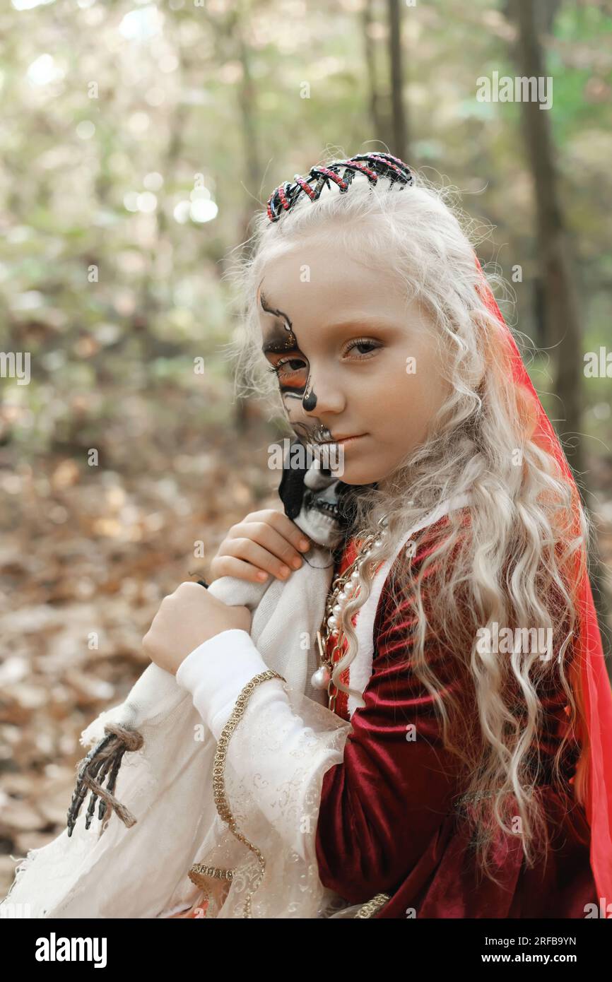 A child girl sits on a stump in the forest in a medieval dress in the ...