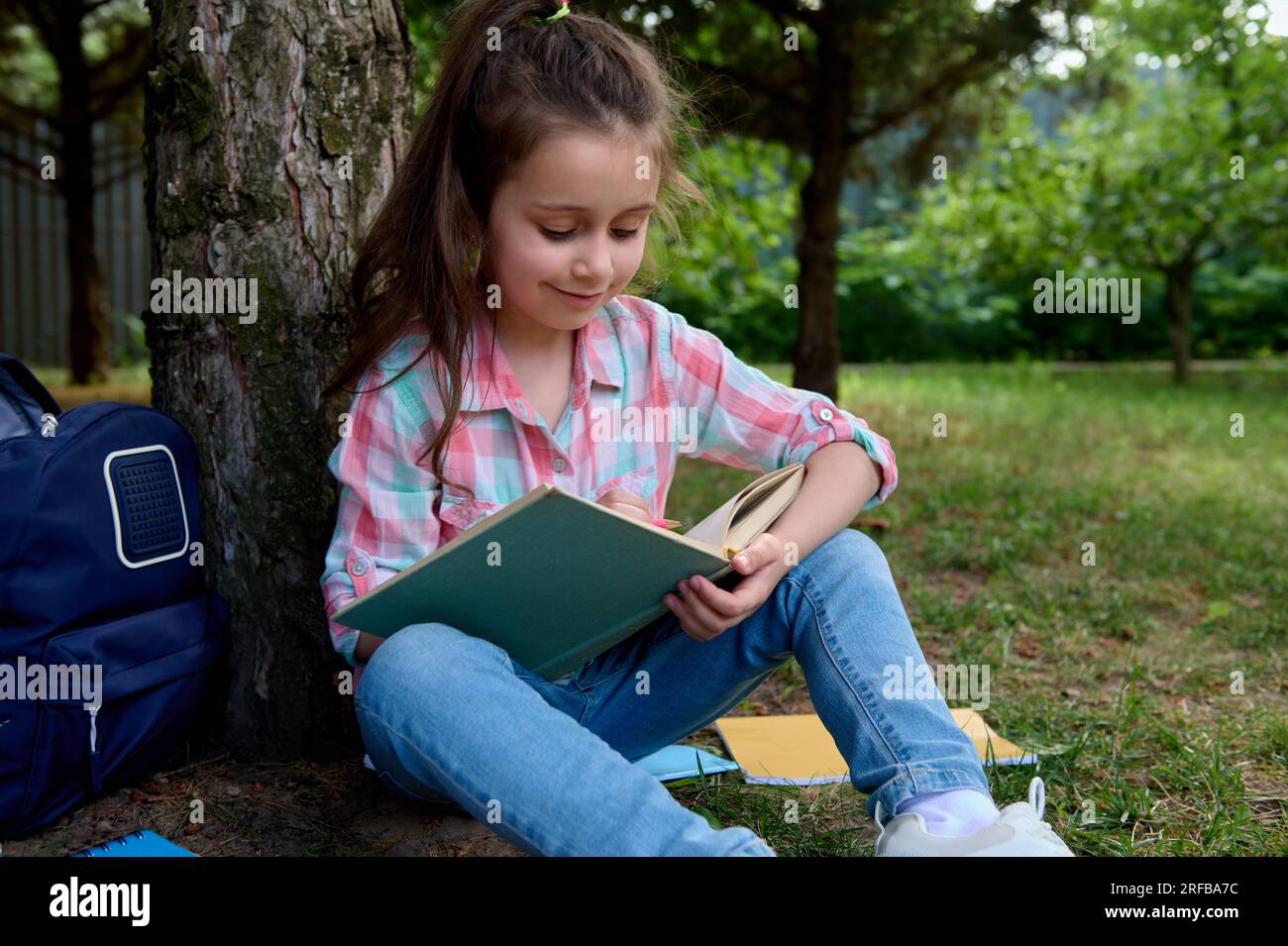 Charming diligent little child girl doing homework in the park, writing ...