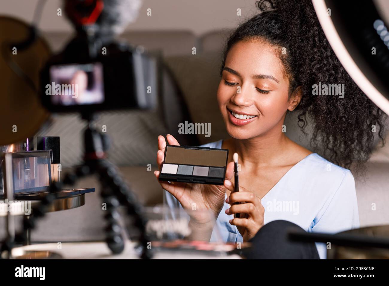 Smiling influencer making a review on eyeshadow palette while sitting ...
