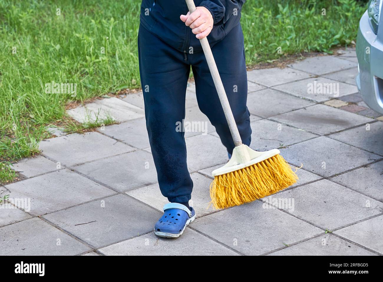 Legs of a man cleaning the house yard concrete slabs with a mop, broom ...