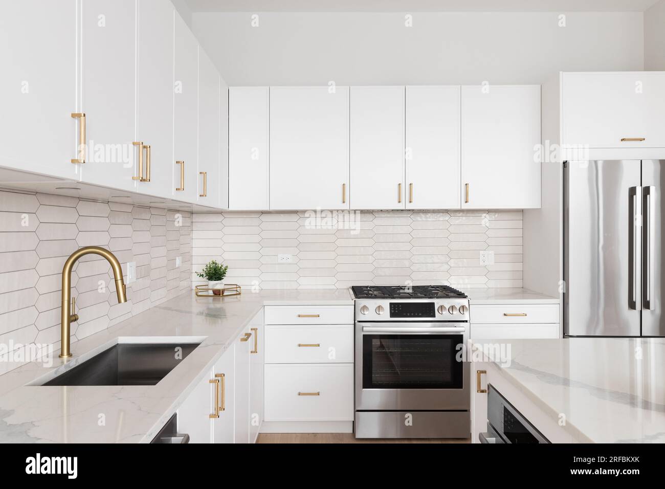 A kitchen detail with white cabinets, gold hardware and faucet, marble ...
