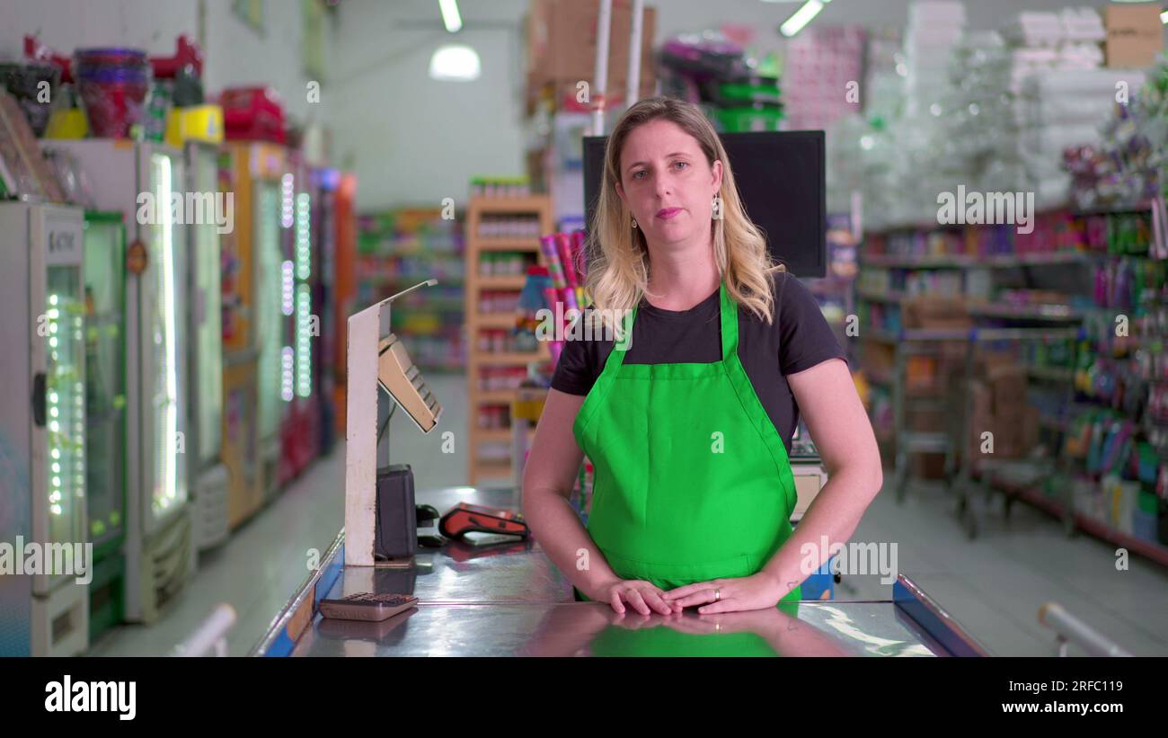 Female employee of Supermarket standing by cashier checkout looking at ...