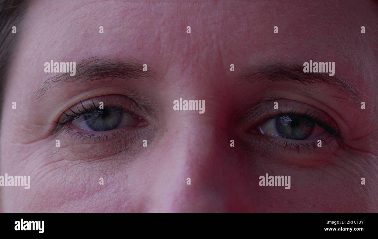 Macro tight close-up of a woman in 40s with blue eyes looking at camera ...