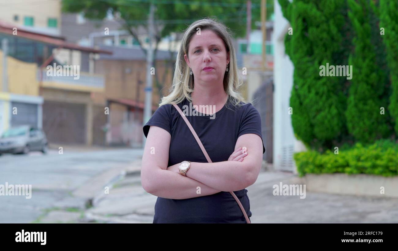 Serious woman standing in street with arms crossed looking at camera in ...