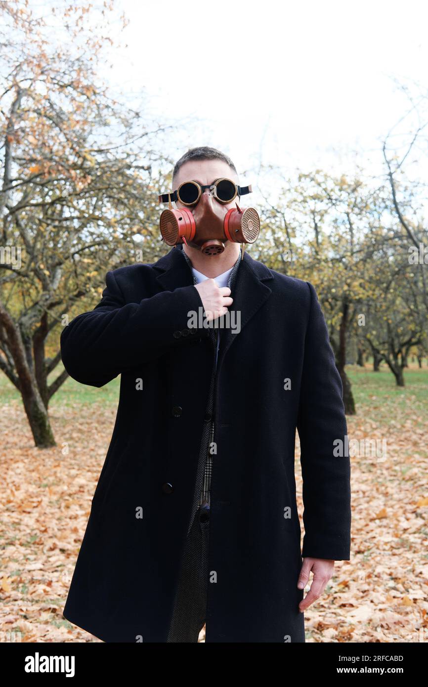 Man in black coat, business suit and gas mask posing in autumn park ...