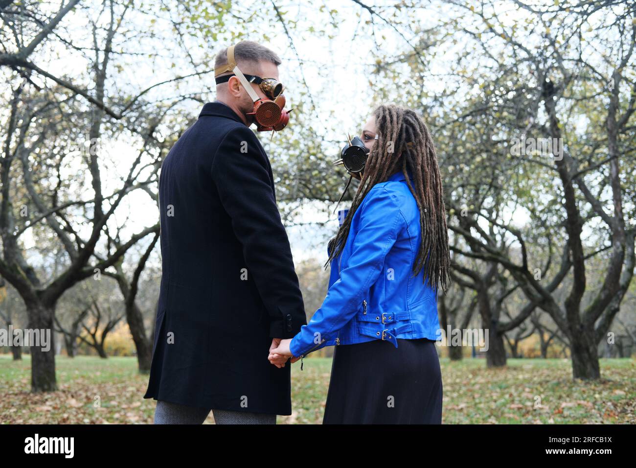 A woman with dreadlocks and a gas mask holds the hand of a man with ...