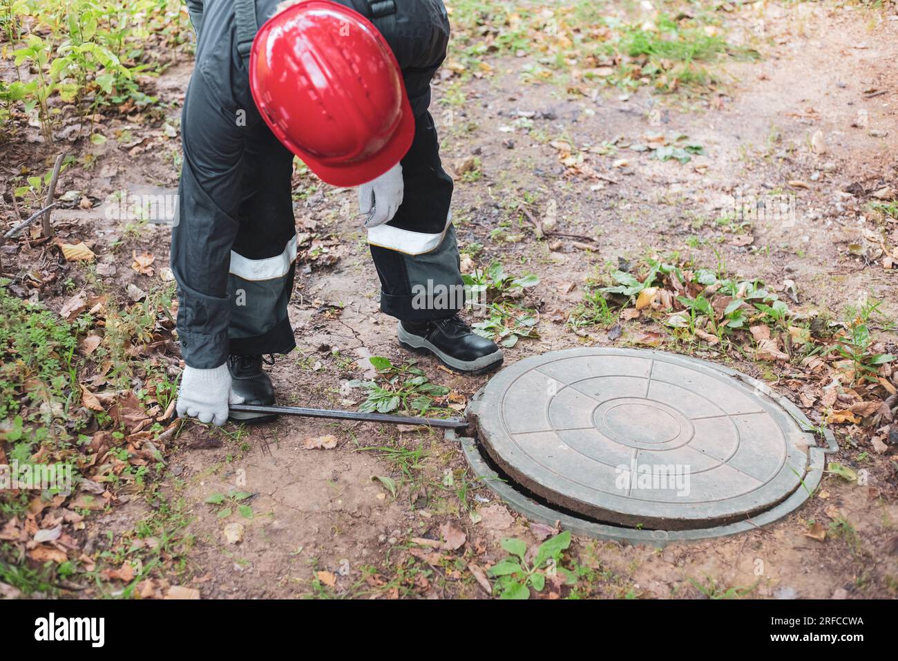 a man in overalls opens a sewer hatch. Cleaning of sewers and drains ...