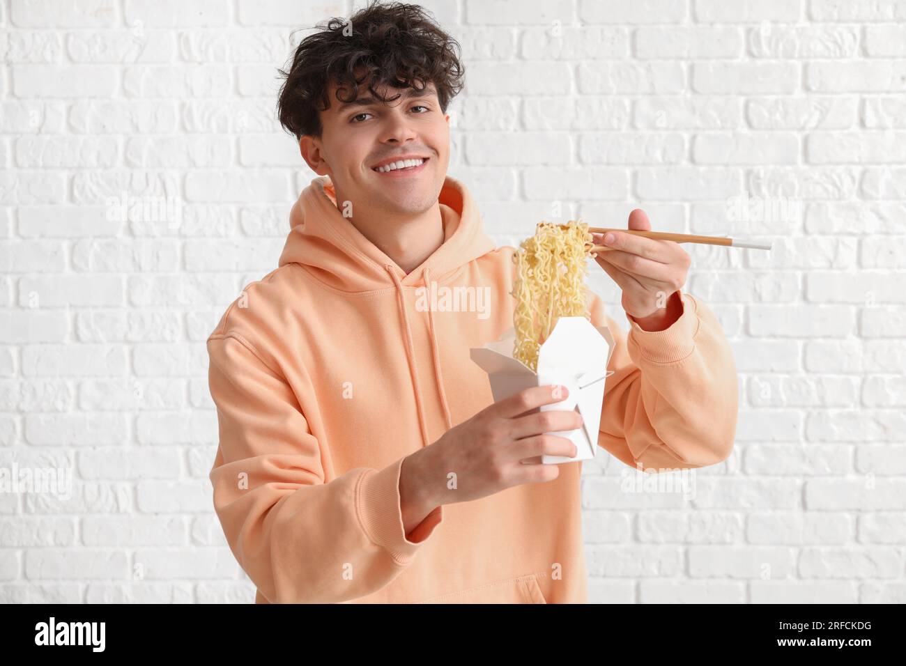 Young man eating tasty Chinese food on white brick background Stock ...