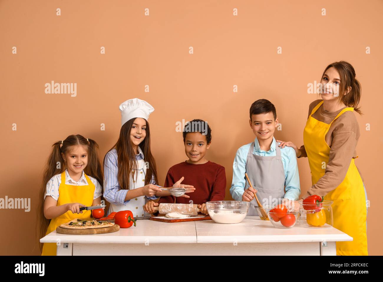 Female chef with group of little children during cooking class on beige ...
