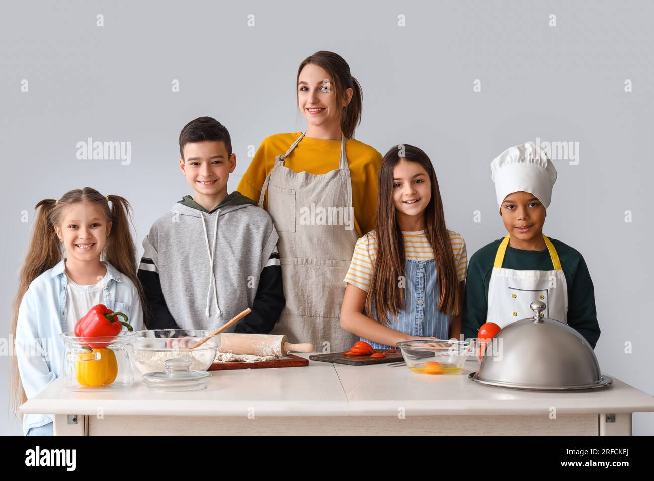 Female chef with group of little children during cooking class on light ...