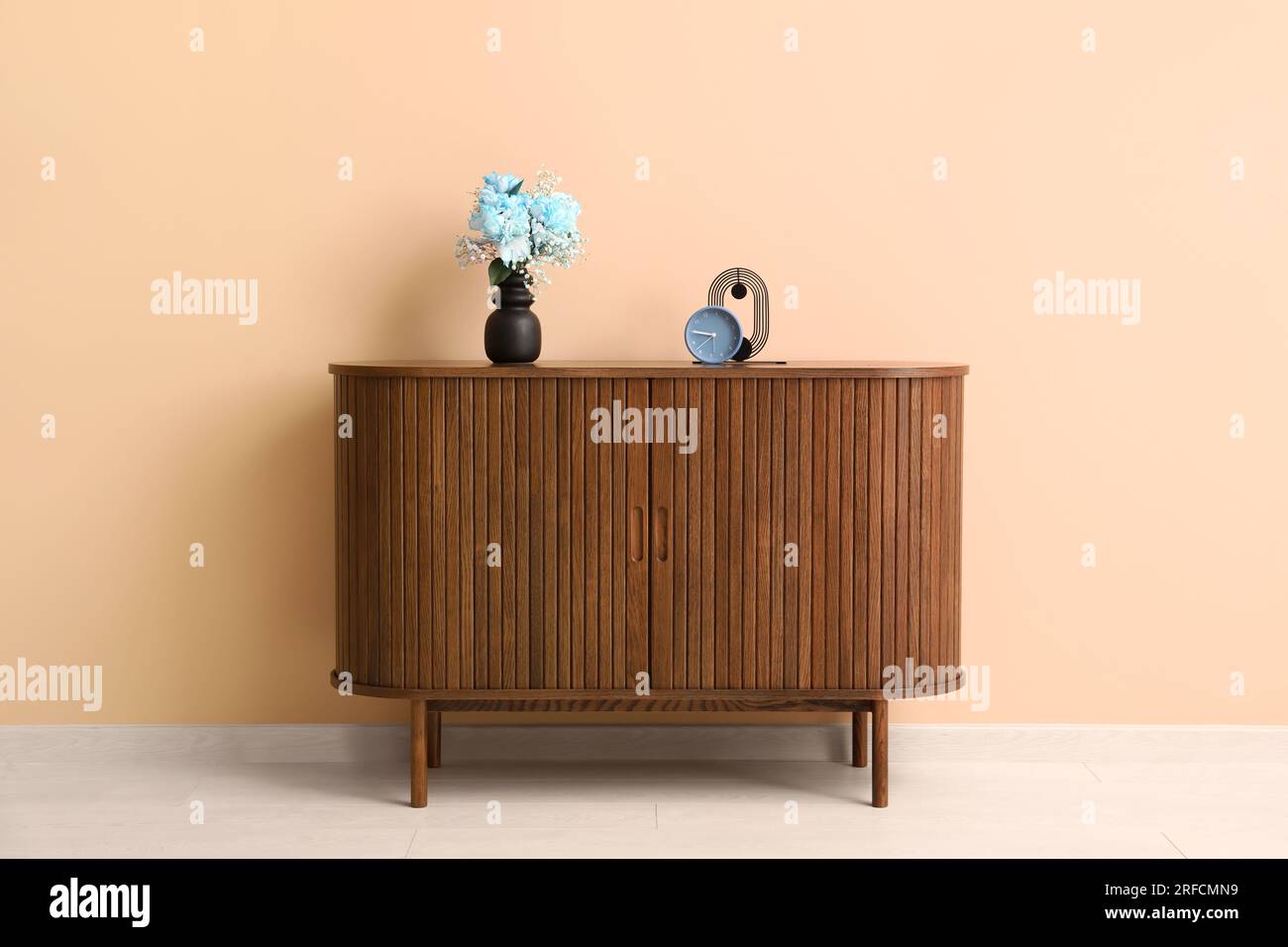 Stylish wooden chest of drawers with flowers and alarm clock near beige ...