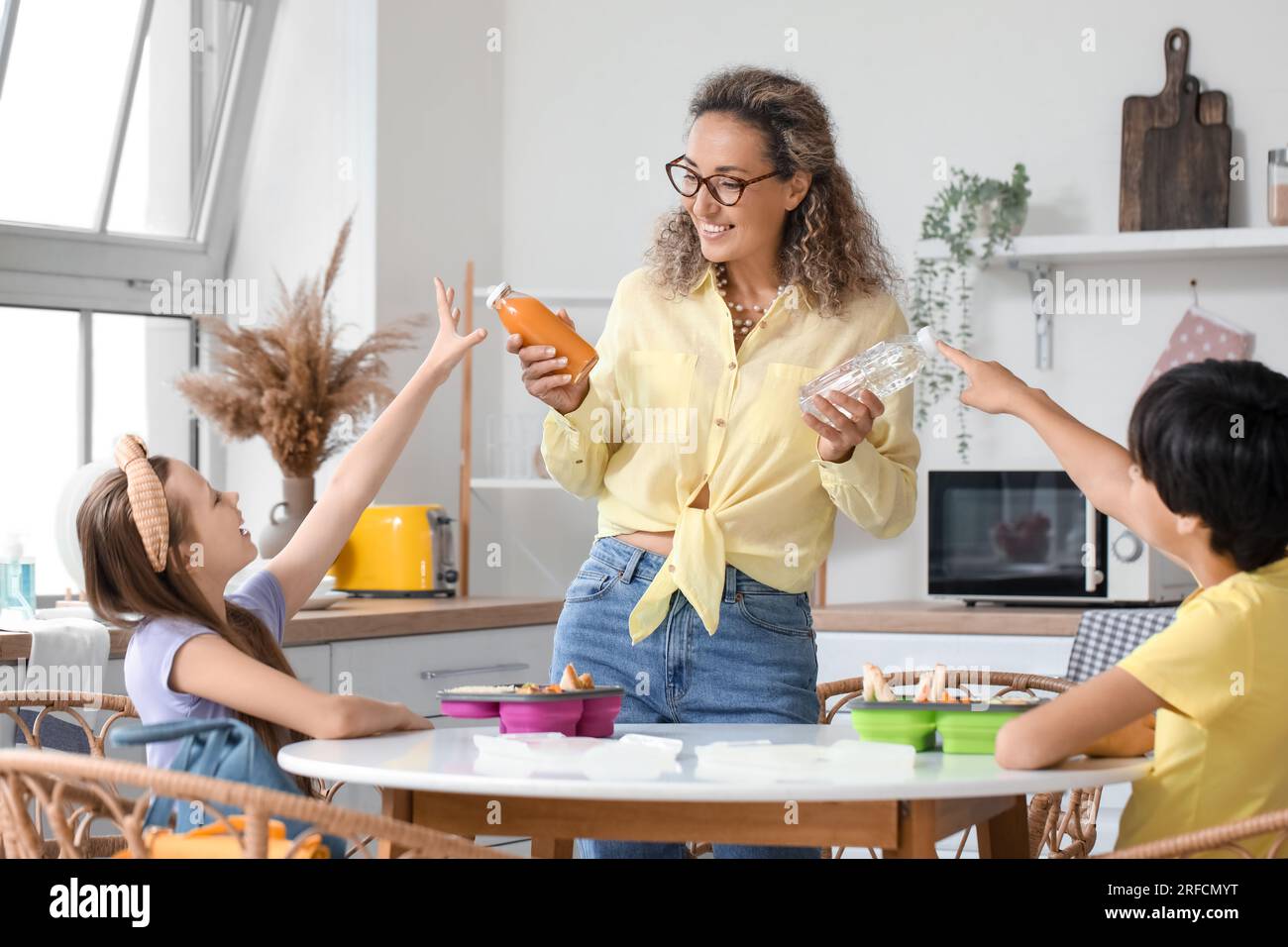 Mother giving drinks to her little children before school in kitchen ...