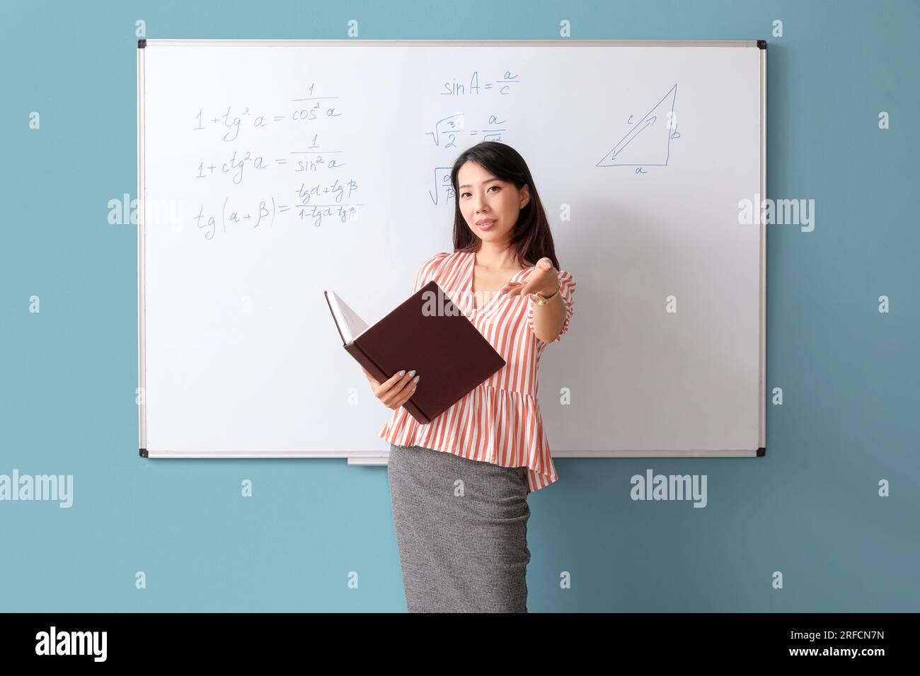 Asian Math teacher with book near flipboard in classroom Stock Photo ...