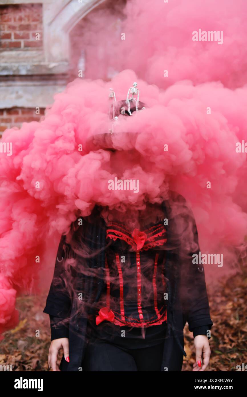 A woman in the guise of Baron Sabbath poses in red smoke. Smoke covers ...