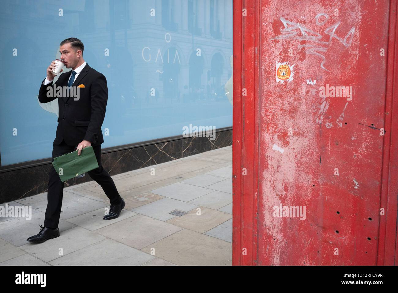 A businessman drinks from a Pret a Manger beverage and walks past a red ...