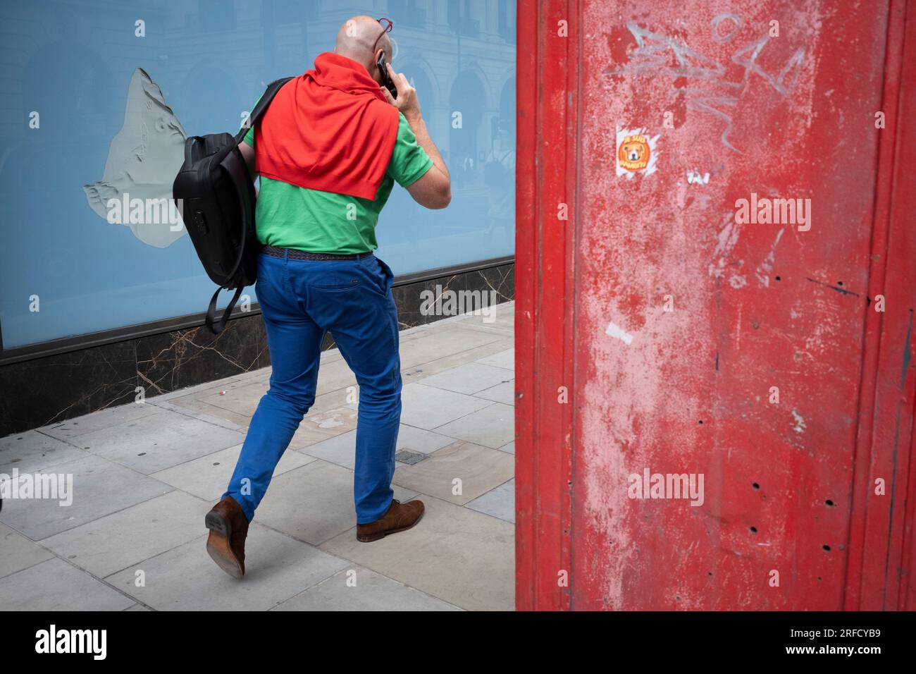 A male pedestrian walks past a red phone box and blue hoarding for a ...