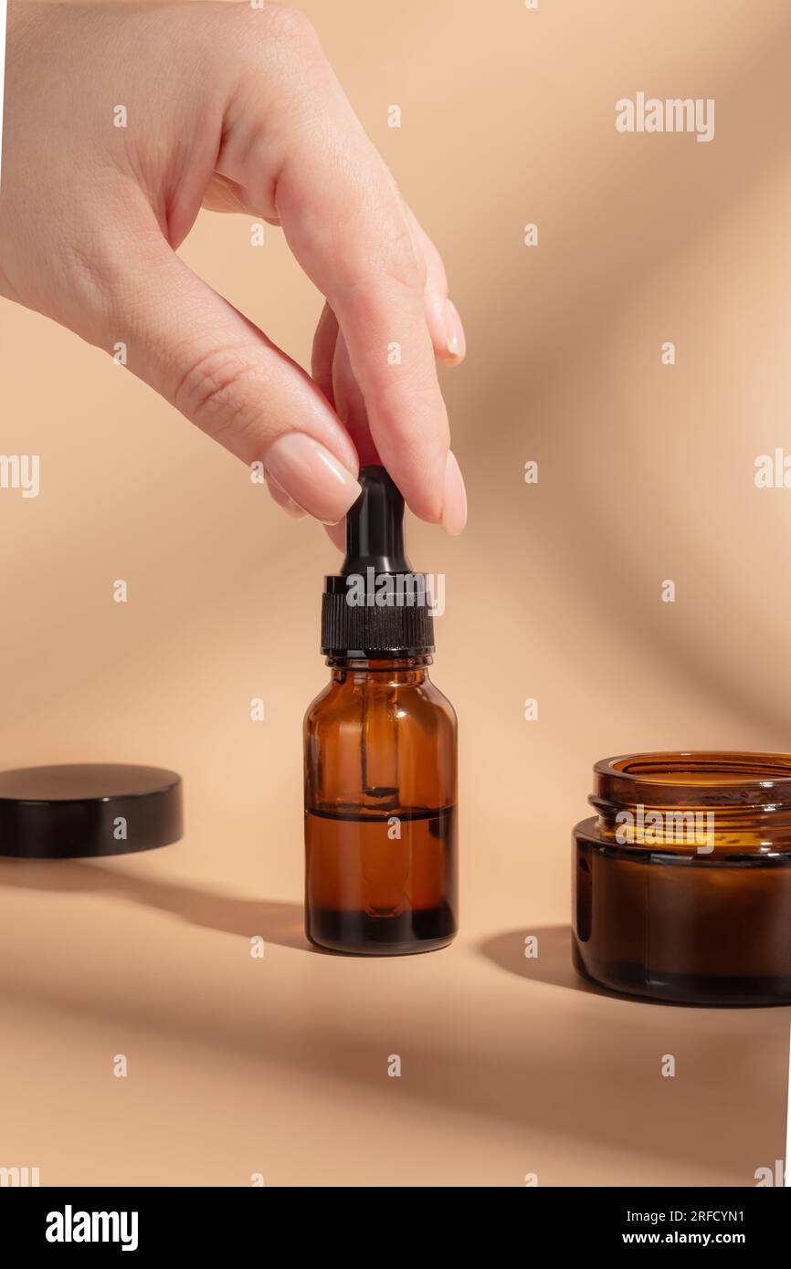 Female hand taking a glass bottle with beauty oil or serum standing ...
