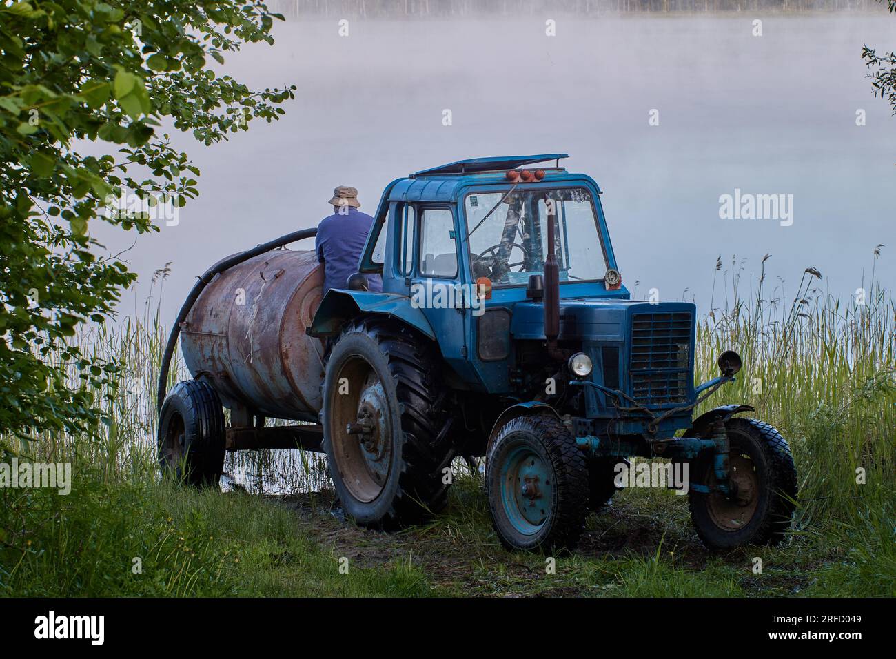Blue wheeled agricultural tractor with tank trailer is refueled with ...